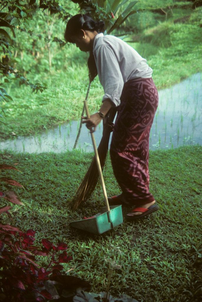 Young woman wearing woven wrapped cloth and shirt sweeps grass at ...