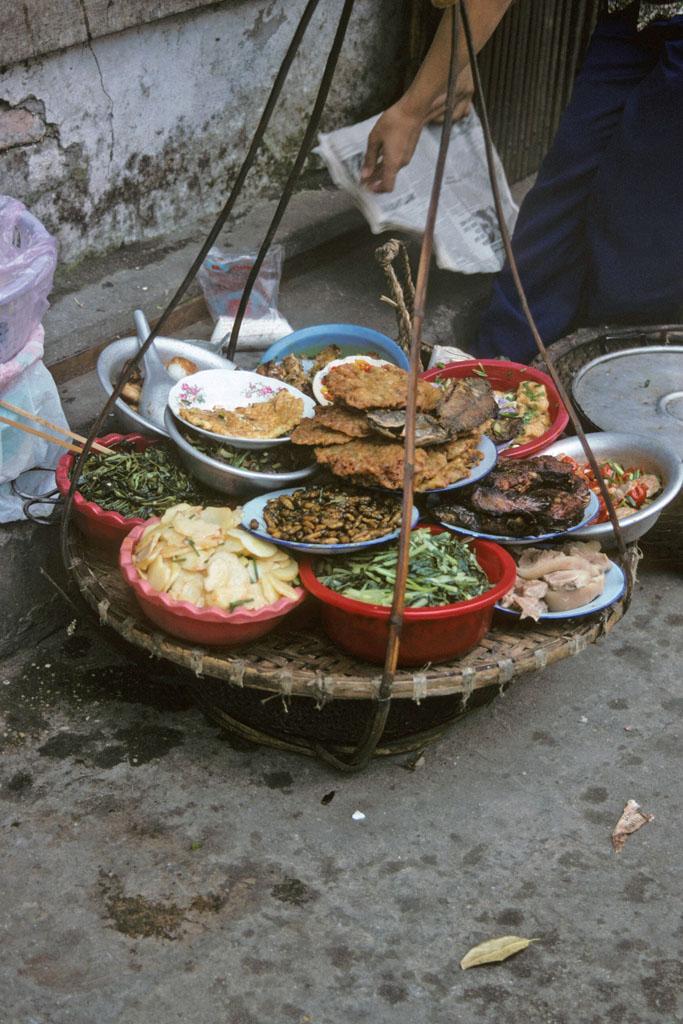 Hanging tray with stacked bowls of prepared foods sold by street vendor ...